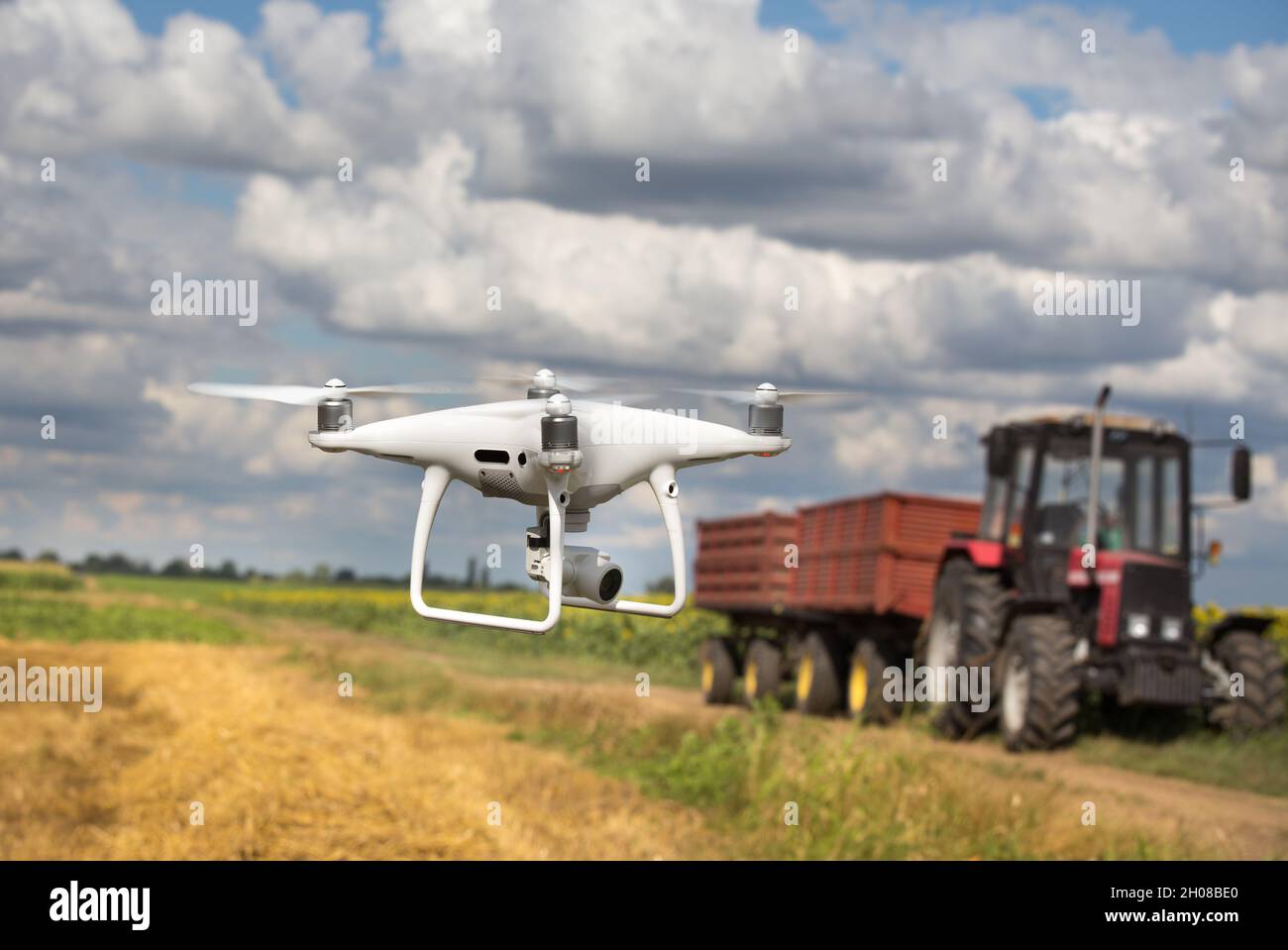 Drone flying in front of tractor with trailer in field in early summer ...