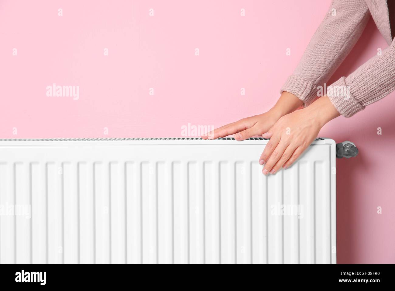 Woman warming hands on heating radiator near color wall Stock Photo - Alamy