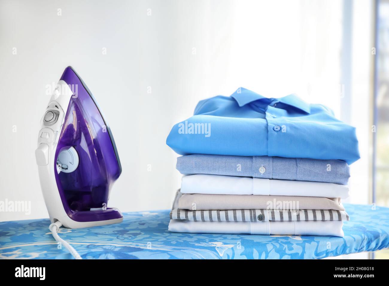 Stack of clean clothes and electric iron on board Stock Photo - Alamy