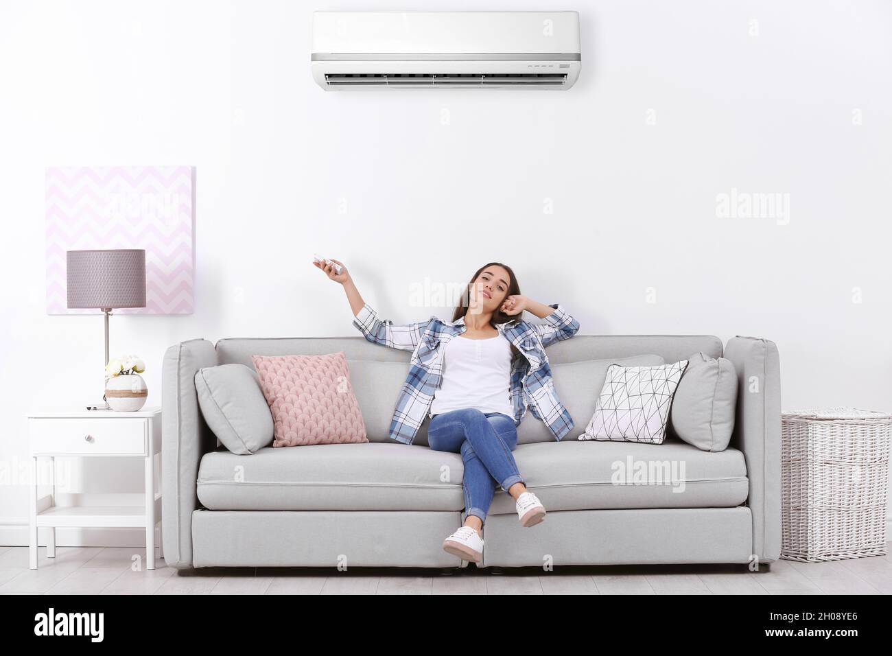 Young woman operating air conditioner while sitting on sofa at home ...