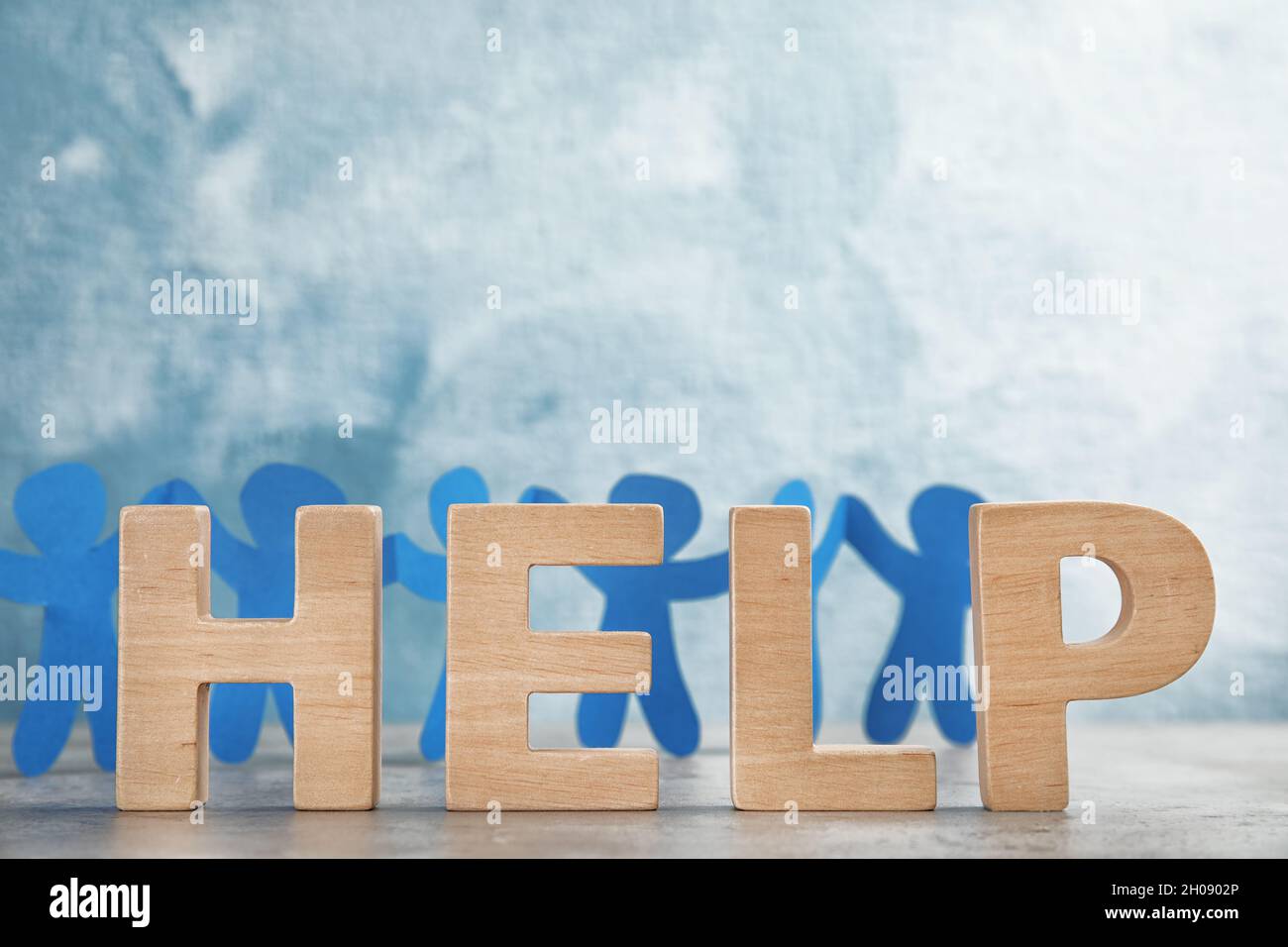 Word "Help" and paper people holding hands on table. Unity concept ...