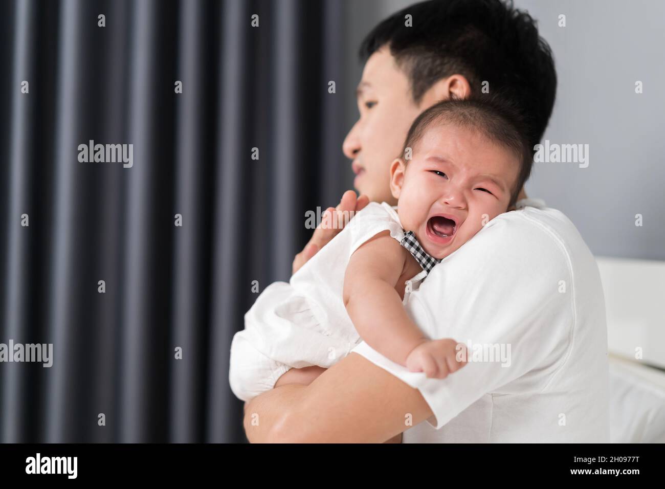 father holding crying baby on a bed Stock Photo - Alamy