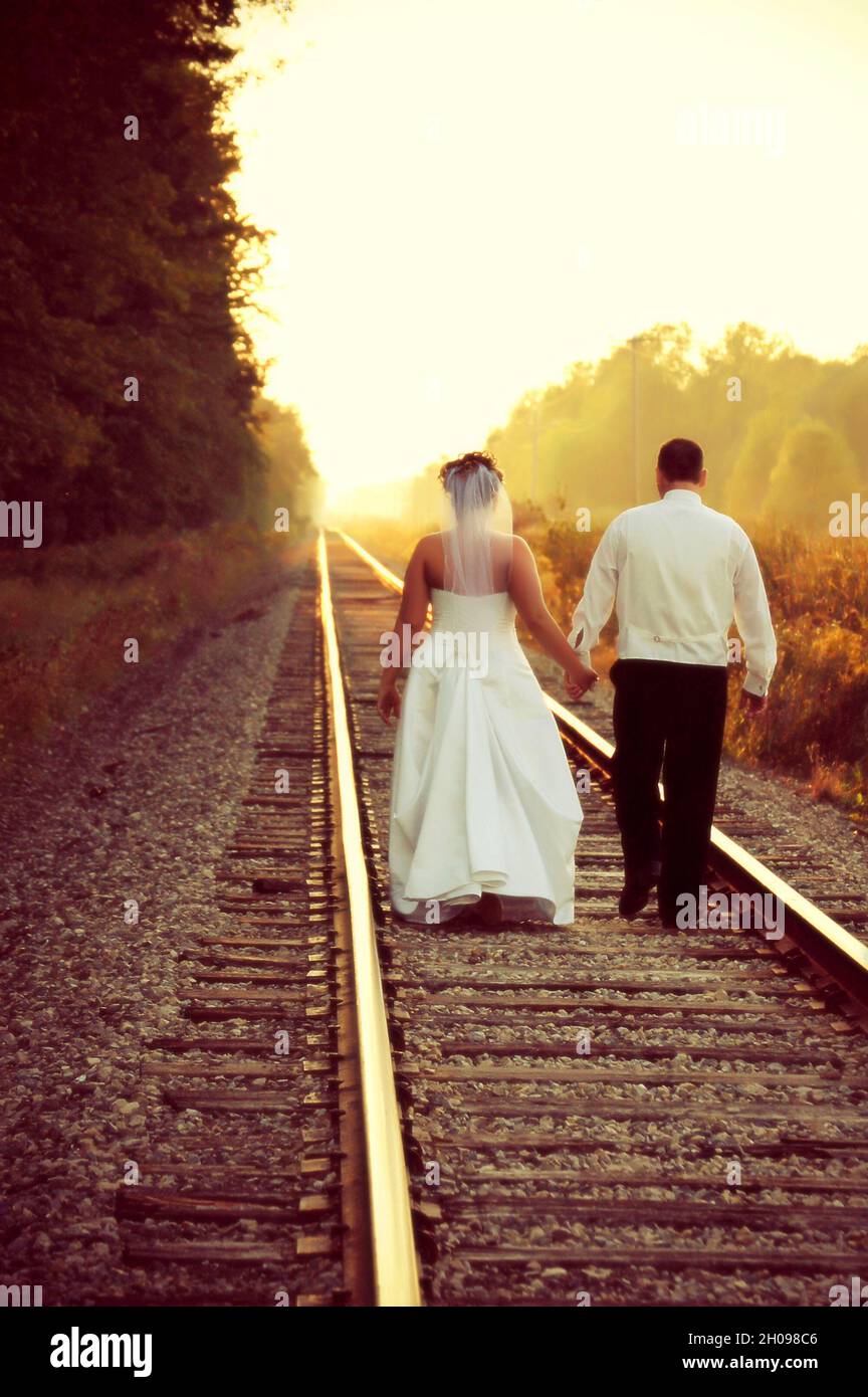 bride and groom walking away holding hands on railroad tracks into ...