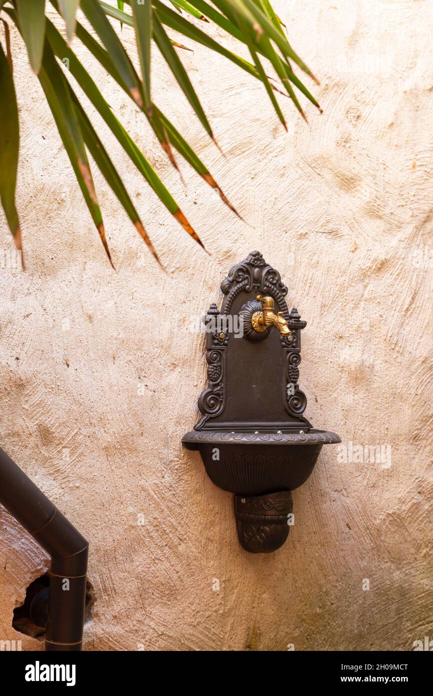 Old ornate brass water tap and basin fixed on a white plastered wall in ...