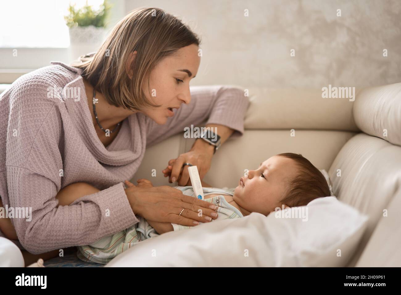 Mother measuring temperature of her ill kid at background. Sick child with high fever lying at ...