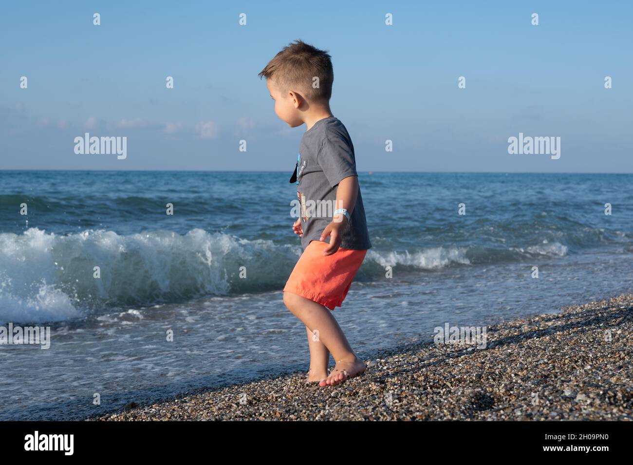 Toddler boy running away from the waves, small boy alone on the beach ...