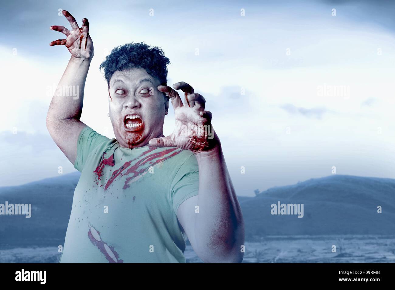 Scary zombie with blood and wound on his body walking on the field ...