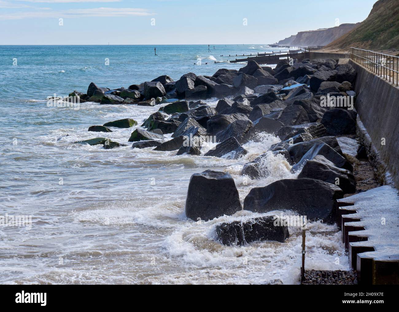 The sea breaks over rocks beyond the end of the promenade at Sheringham ...