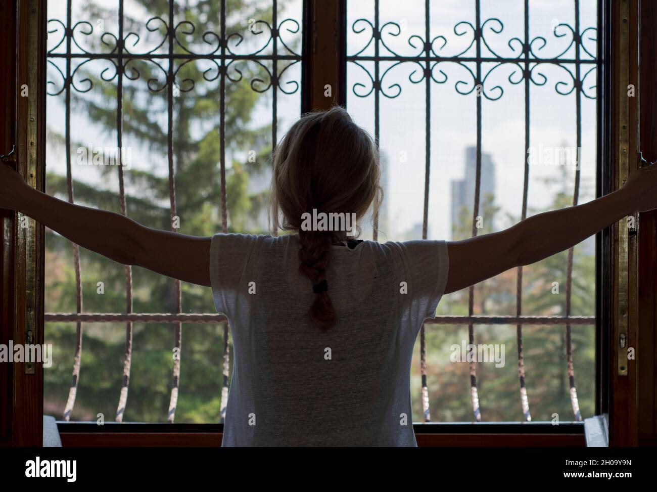 The young woman watches the garden of her house through the barred ...