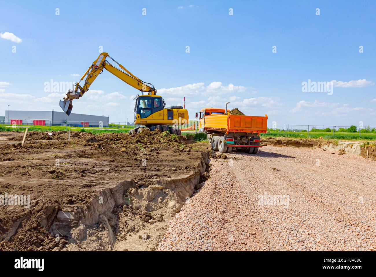 Wheeled excavator is excavating soil and filling a dumper truck with ...