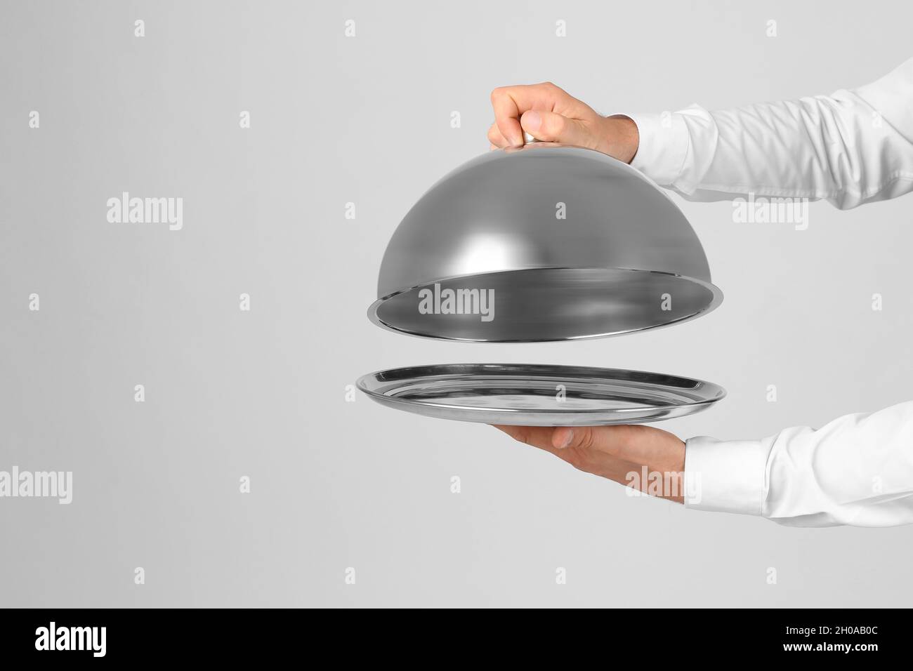 Waiter holding metal tray with lid on light background Stock Photo - Alamy