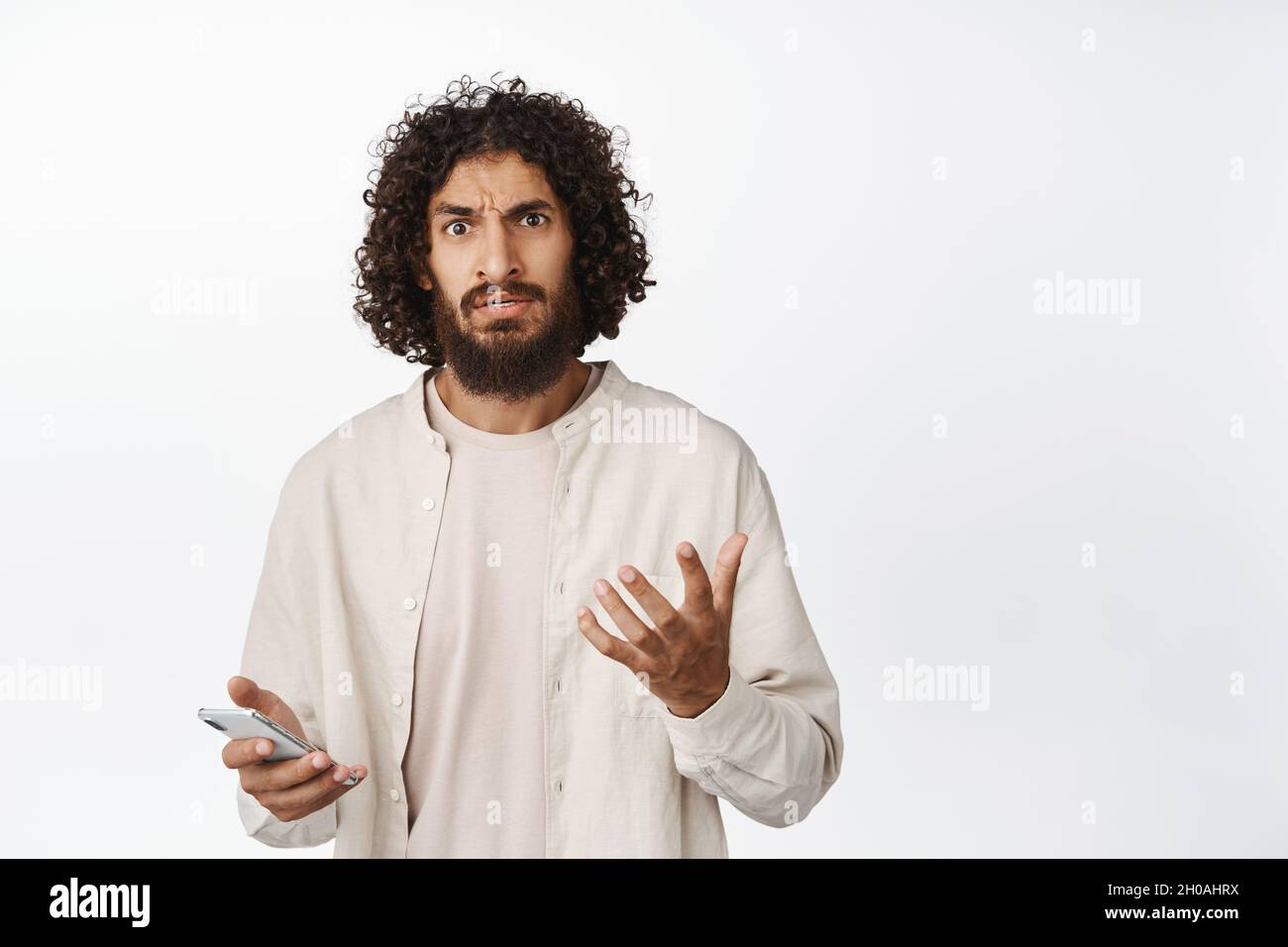Portrait of man holding mobile phone with frustrated and confused face ...