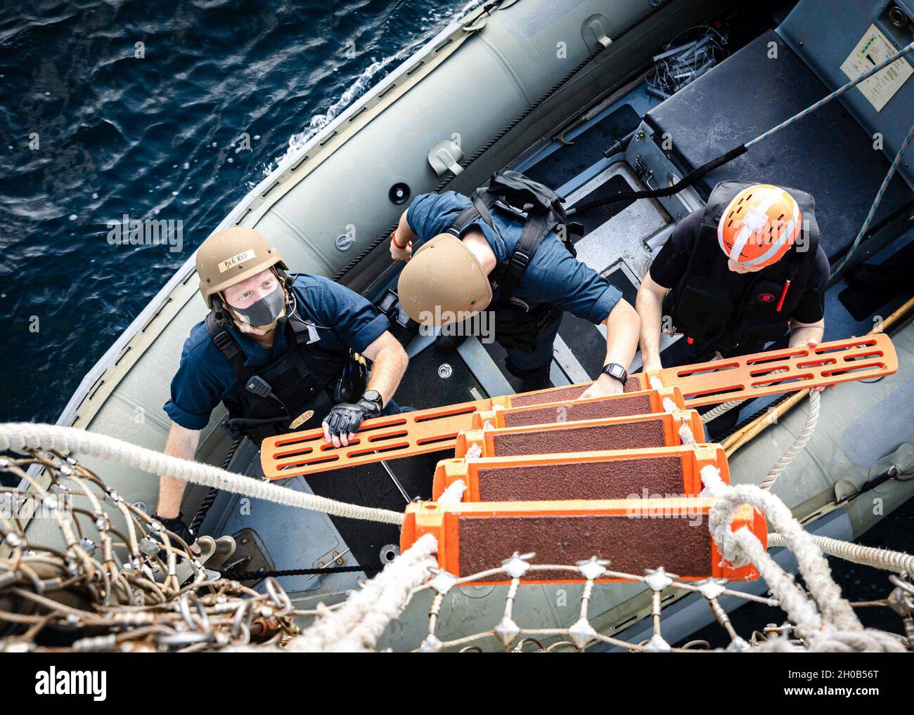 Sailors embark a rigid hull inflatable boat using a pilot’s ladder ...