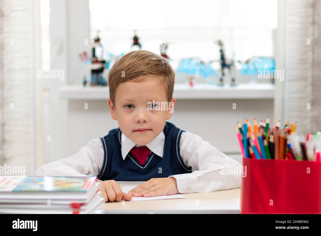 A cute first-grader boy in a school uniform at home while isolated at ...