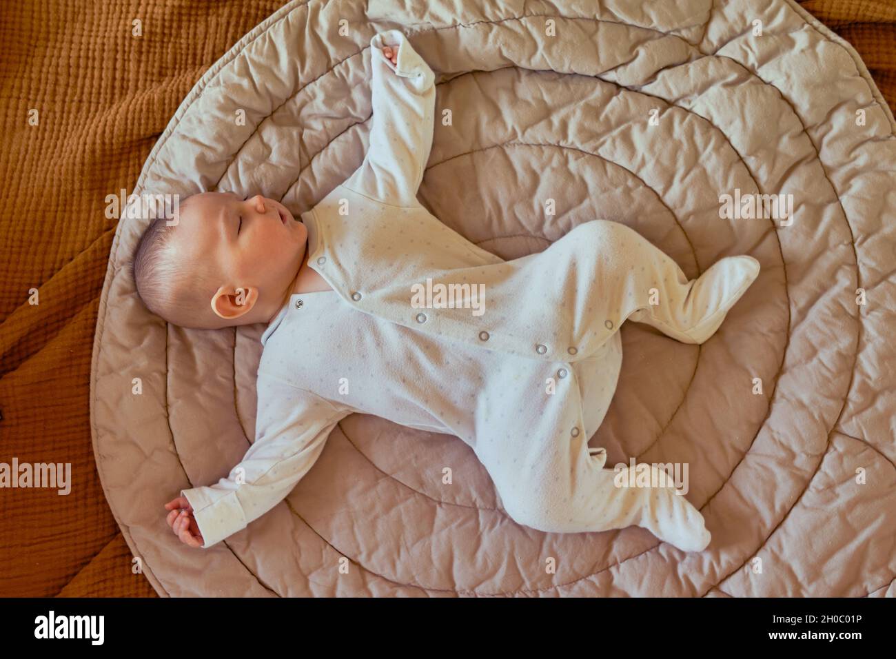 The infant baby sleeps in the frog pose on the mat, top view. The child ...
