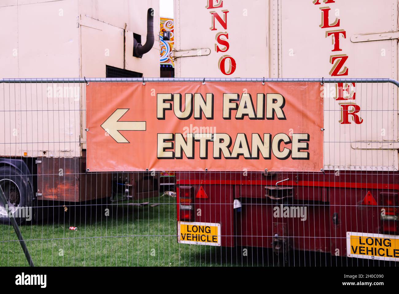 Fun Fair entrance sign on metal fencing behind waltzer lorry ...