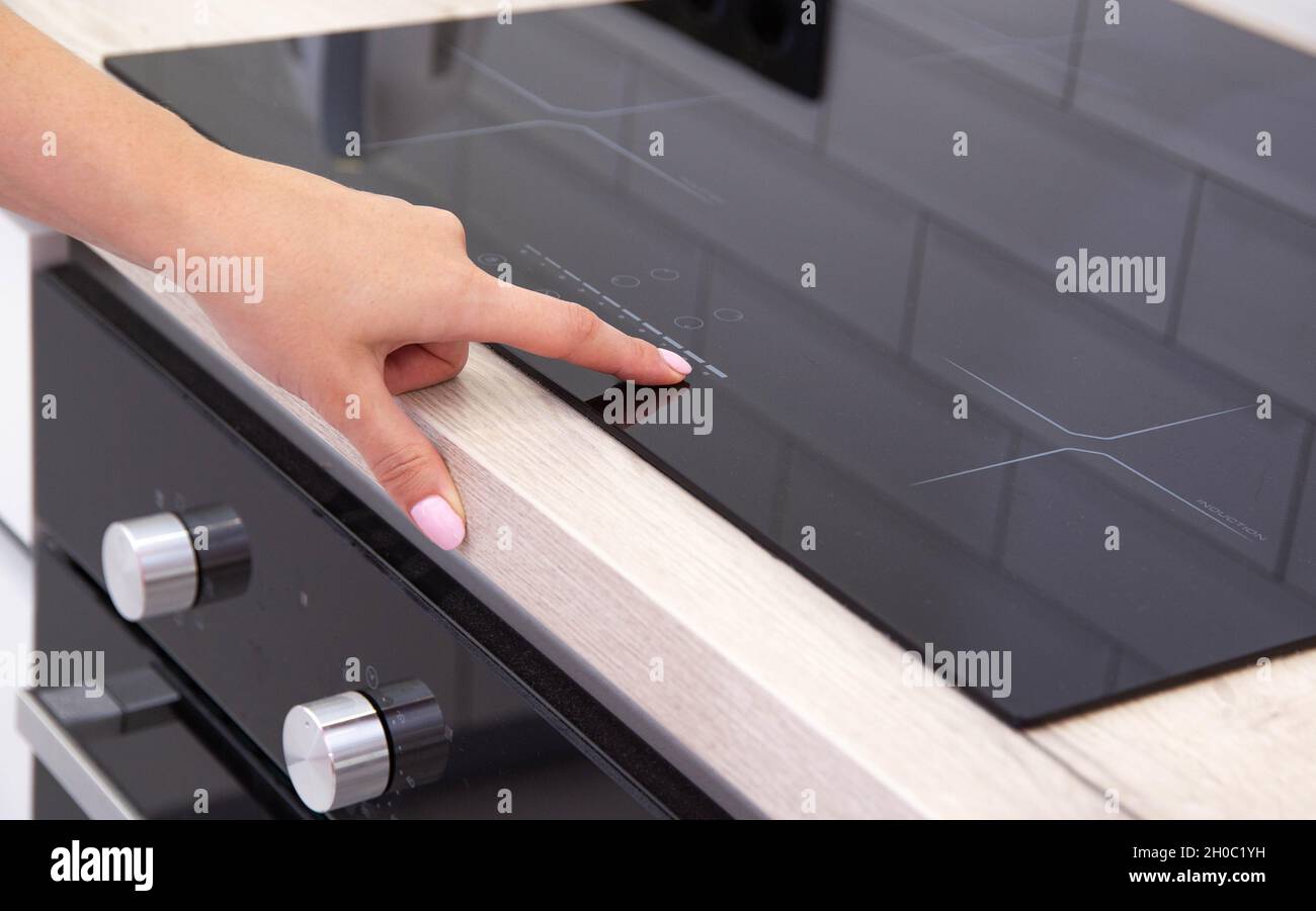 Modern induction ceramic hob with 4 cooking zones. Woman presses hand ...