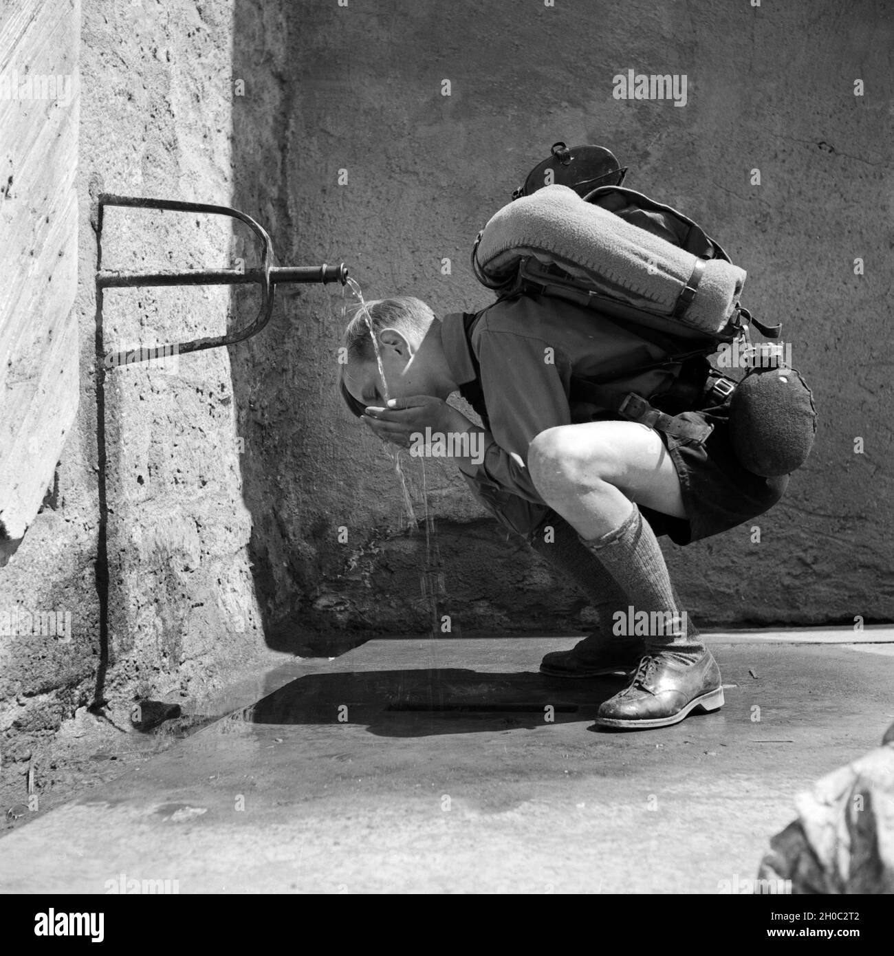 Ein Hitlerjunge trinkt auf einer Wanderung aus einem Brunnenwasserhahn ...
