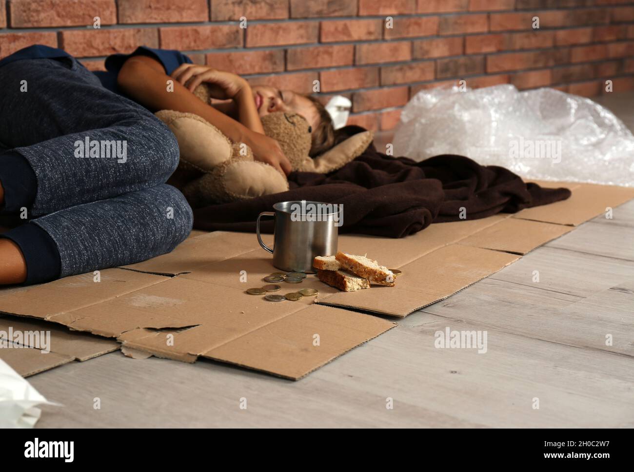 Poor homeless boy sleeping with his toy on floor near brick wall Stock ...