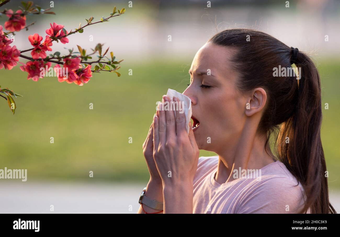 Young pretty woman sneezing in front of blooming tree. Spring allergy ...