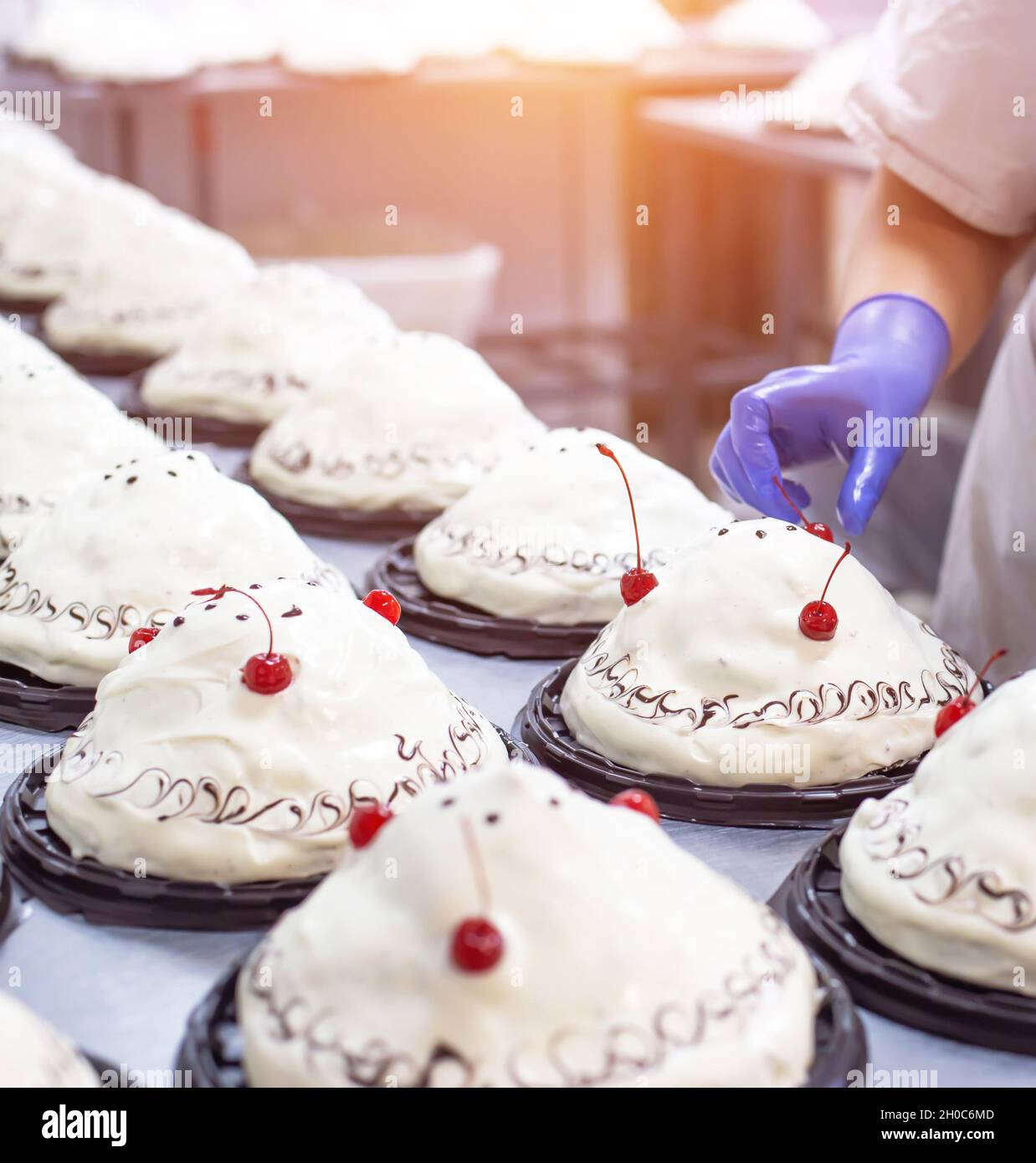 A chef decorates cakes in a confectionery factory with fresh cherry ...
