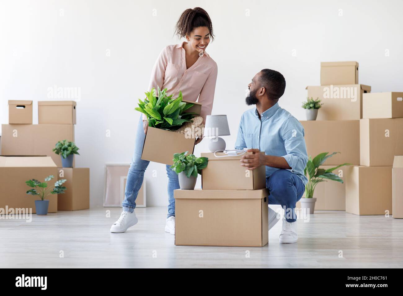 Smiling millennial black husband and wife unpack cardboard boxes in ...