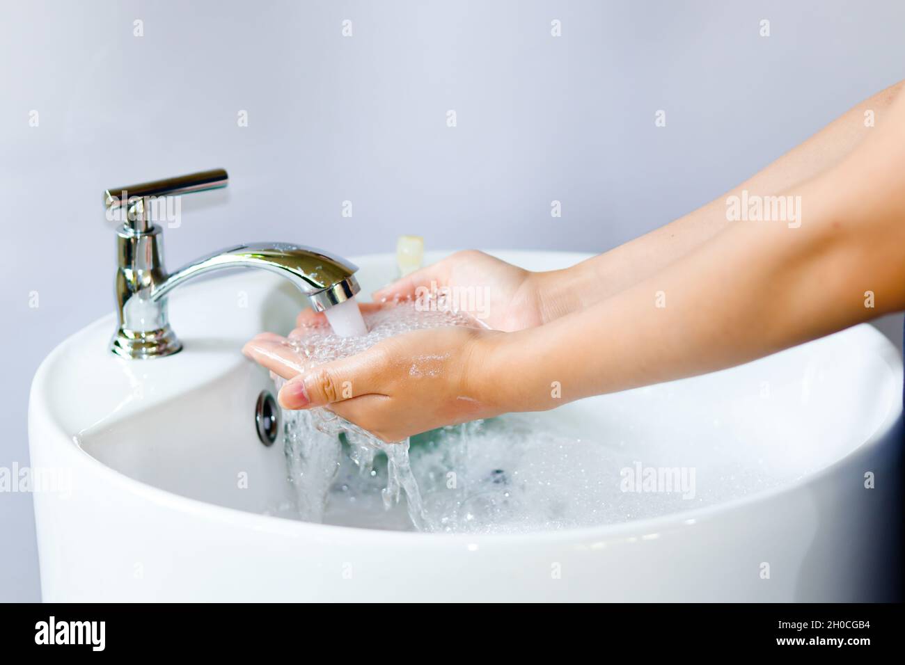 Washing hands in a round white ceramic basin, soap bubbles on hand ...