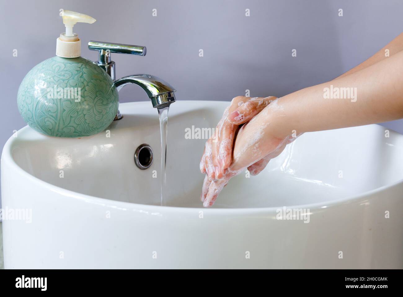 Washing hands in a round white ceramic basin, soap bubbles on hand ...