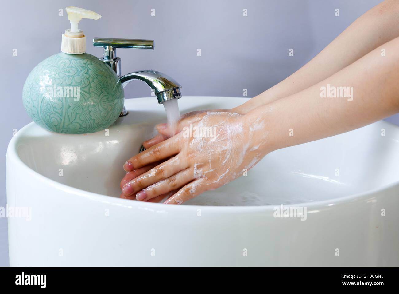 Washing hands in a round white ceramic basin, soap bubbles on hand ...