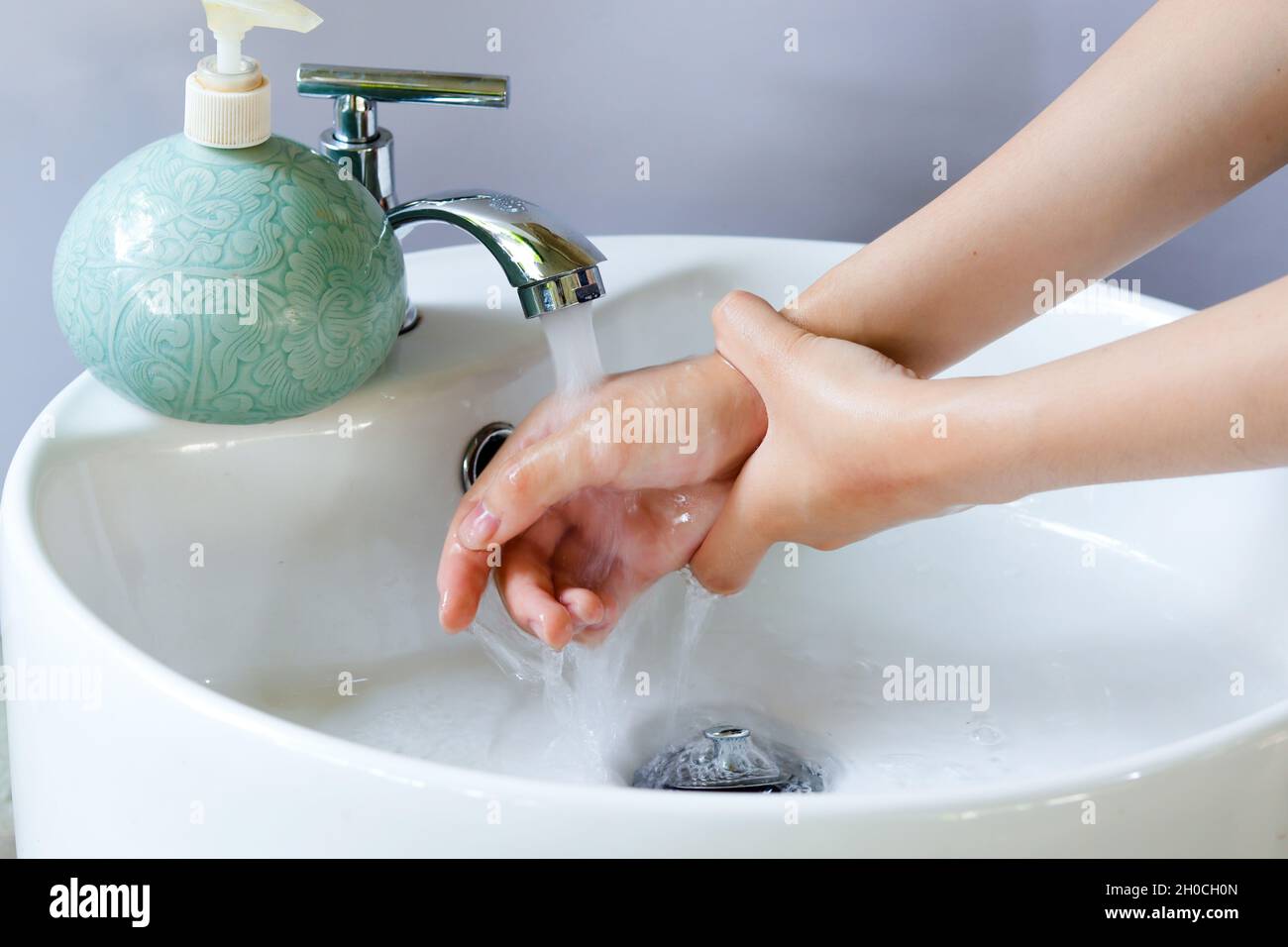 Washing hands in a round white ceramic basin, soap bubbles on hand ...