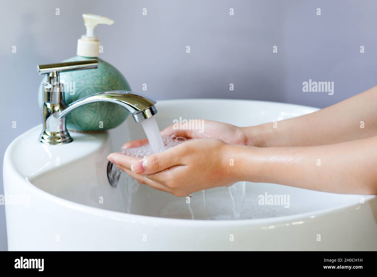 Washing hands in a round white ceramic basin, soap bubbles on hand ...