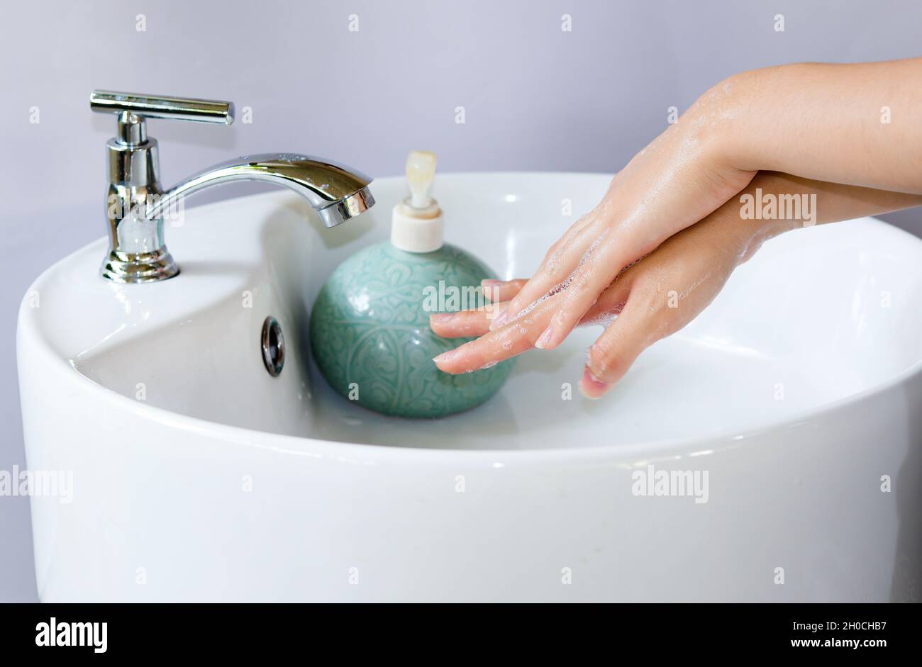 Washing hands in a round white ceramic basin, soap bubbles on hand ...