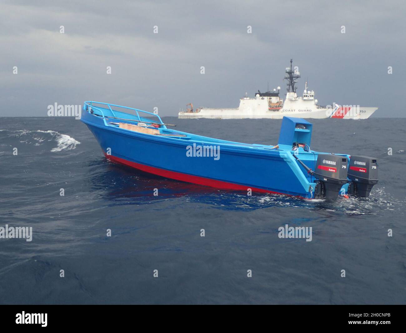 A panga-style vessel is shown in front of The Coast Guard Cutter ...