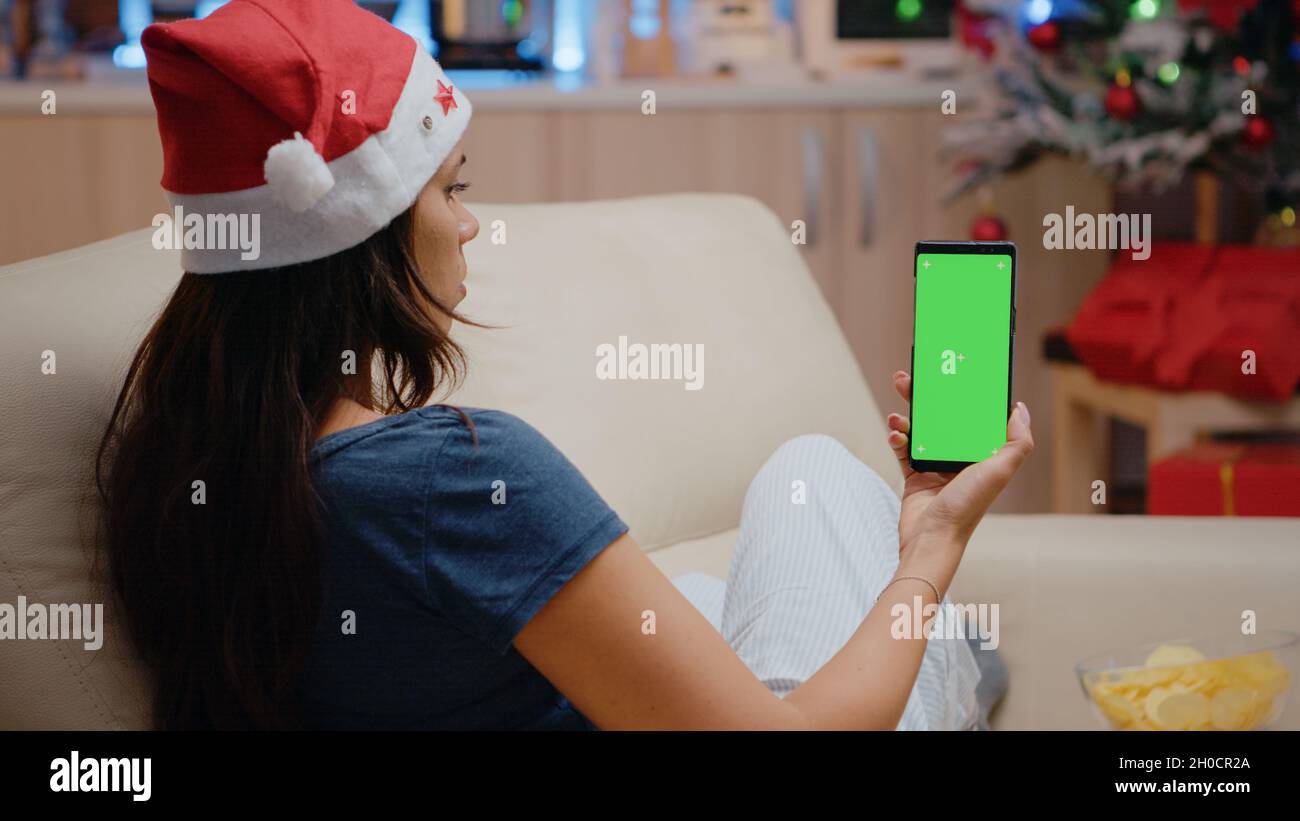 Woman vertically holding smartphone with green screen on christmas eve ...