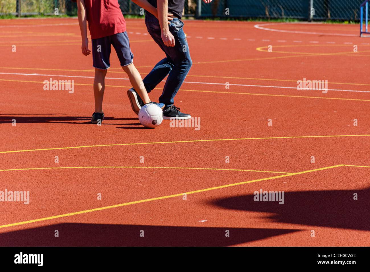 Low section photo of father and son playing soccer on orange sports ...