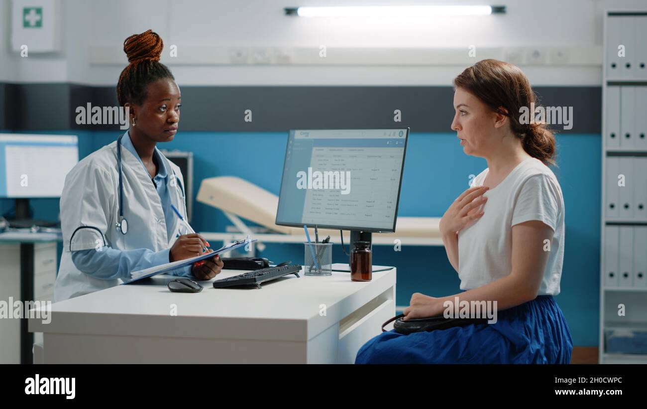 Doctor taking notes on checkup papers and talking to sick patient in ...