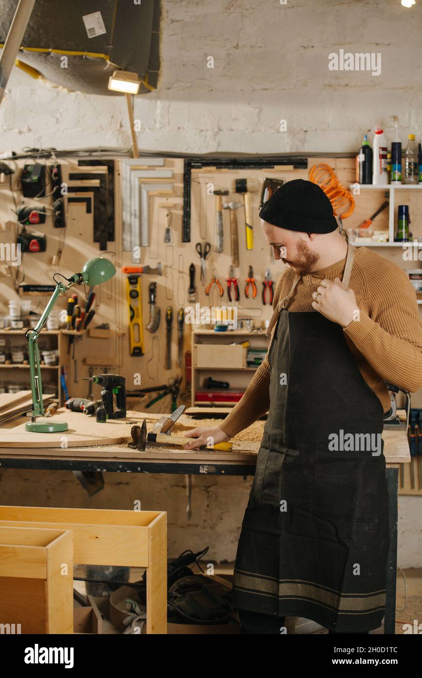 Middle aged carpenter in a watch cap holding a hammer, in a big ...