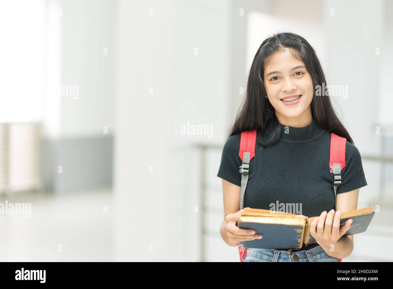 Young cheerful Southeast-Asian female college student carrying book ...