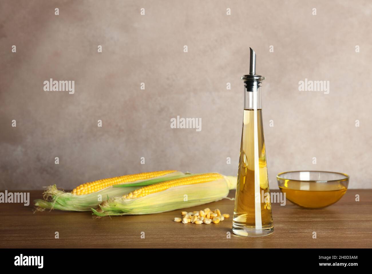 Bottle with fresh corn oil and cobs on table against color wall Stock ...
