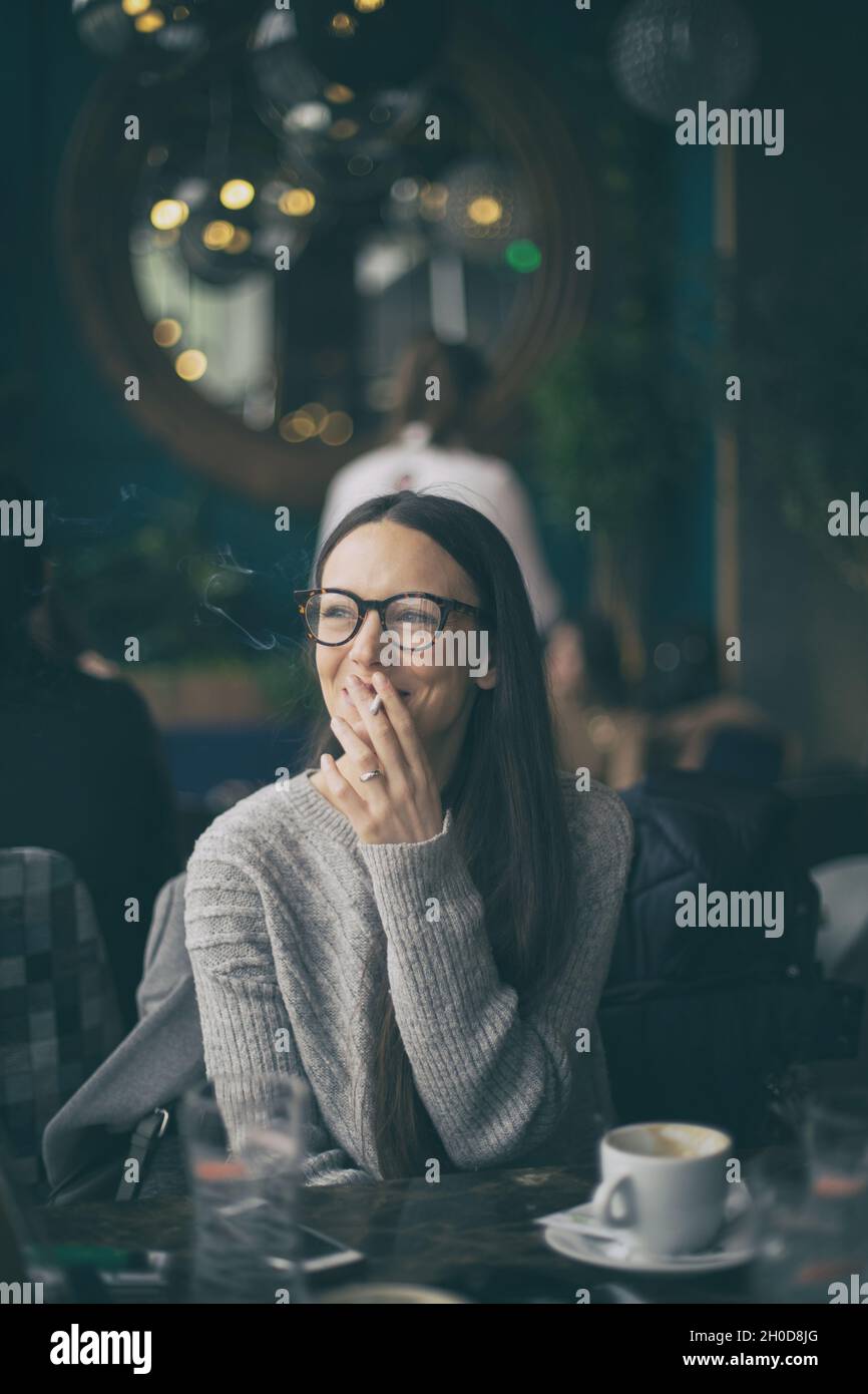 Girl sitting in cafe drinking coffee, smoking cigarette and talking to ...