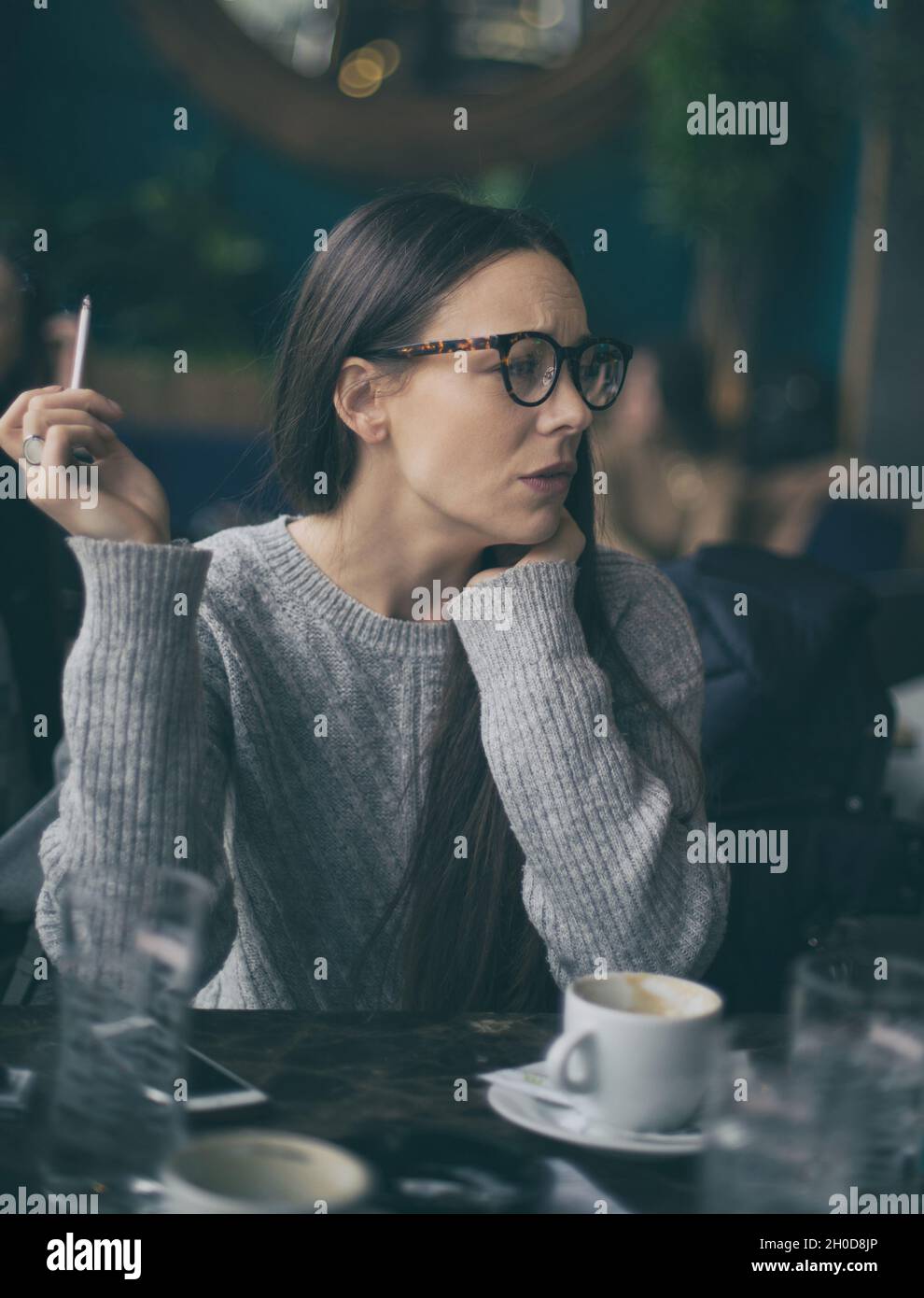 Girl sitting in cafe drinking coffee, smoking cigarette and talking to ...