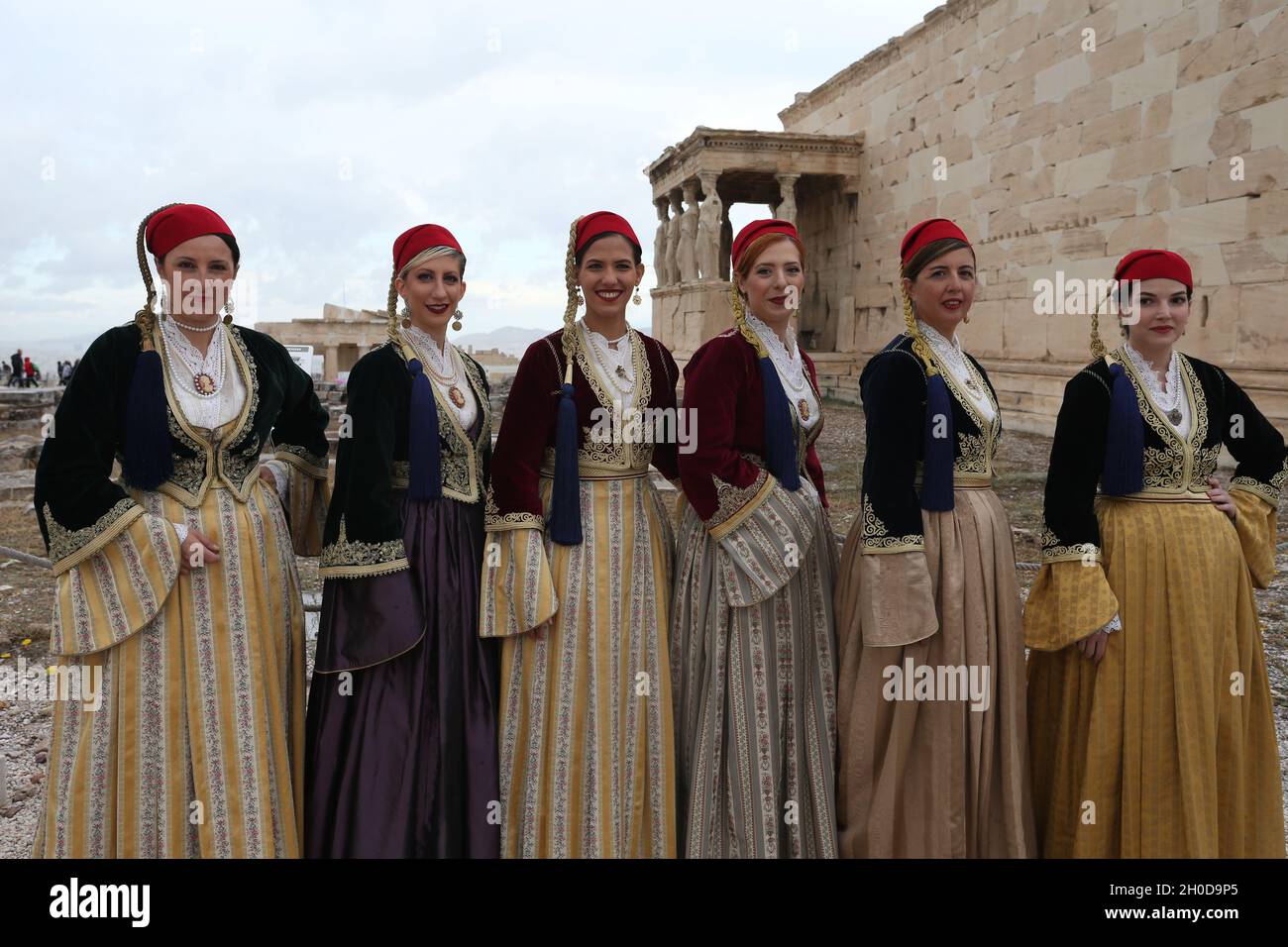 Women in traditional local costumes carry a Greek flag to the flag pole ...