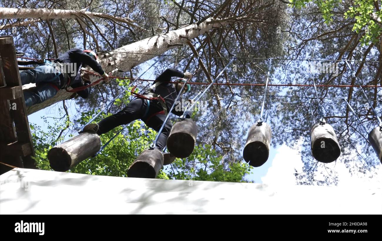 Young men passes obstacles in adventure park in forest. Stock. Men pass ...