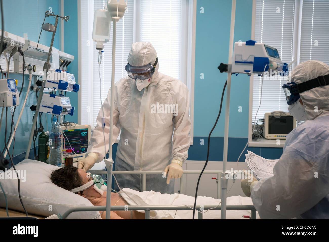 Doctor in a protective suit puts a respiratory mask on a patient with a ...