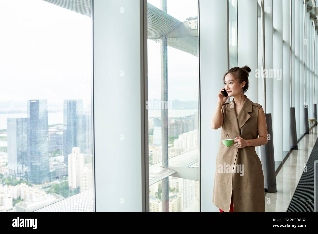 mature asian woman standing by the window talking on mobile phone ...