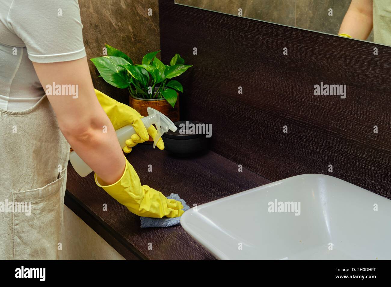 A woman is cleaning the bathroom by wiping it with a countertop rag ...