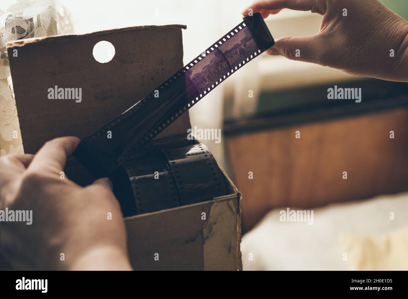 Women's hands hold an old photographic film over a cardboard box with ...