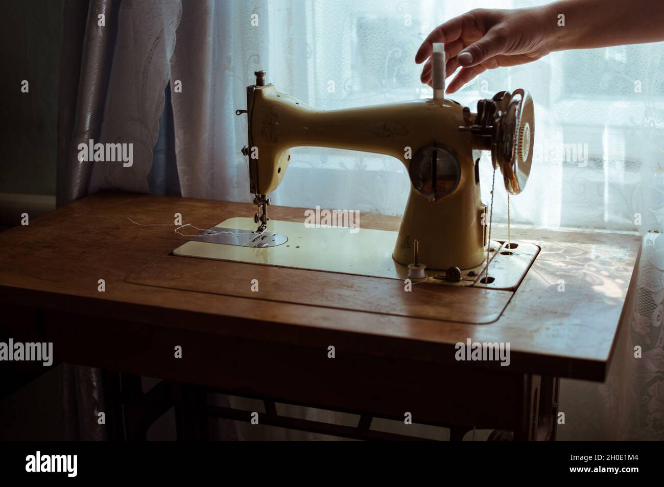 A hand takes a spool of thread from an old retro sewing machine in a ...
