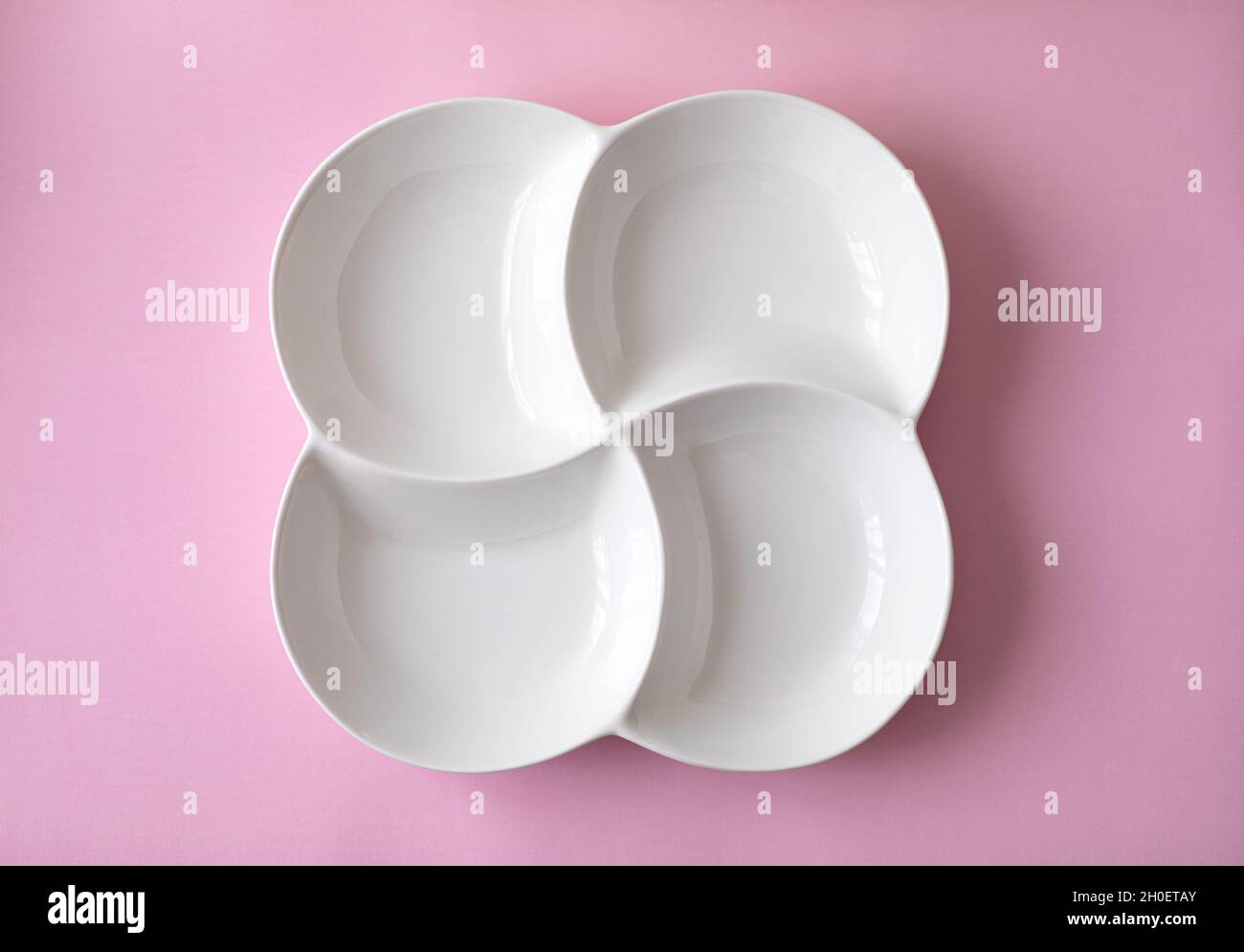 A white four-course dinner plate with a soft shadow on a light pink ...