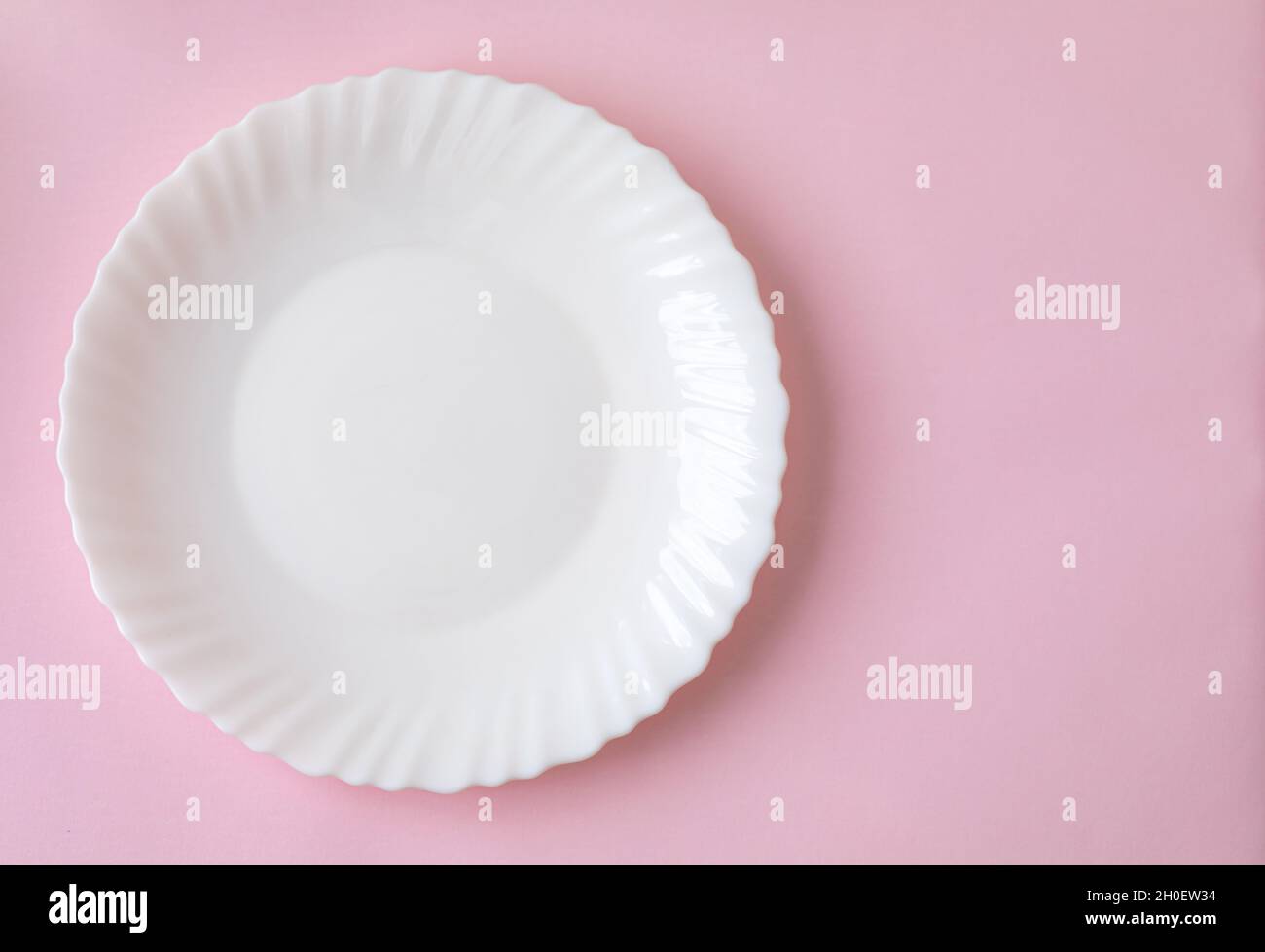 White dinner plate with soft shadow on a light pink surface background ...